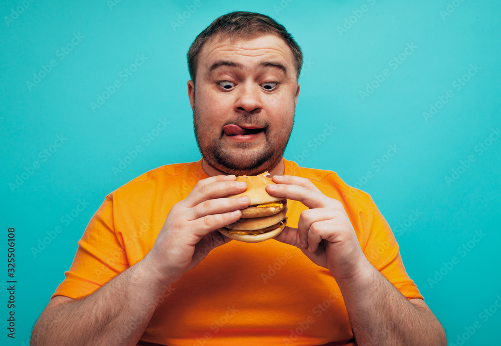 Emotional happy fat man on a blue background eating fast food ...