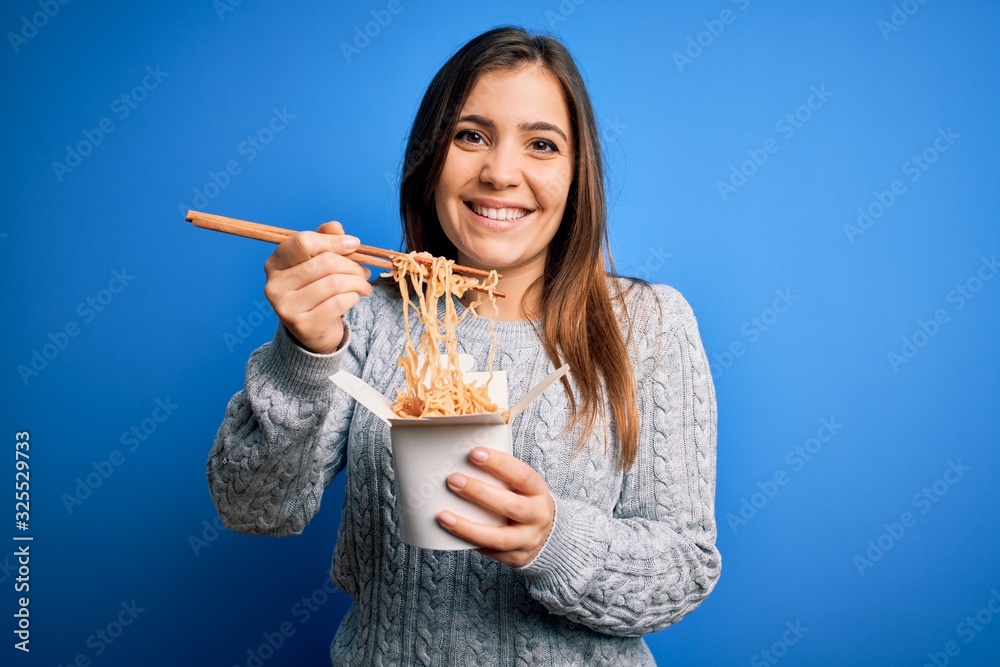 Young woman eating asian noodles from take away box using chopstick ...