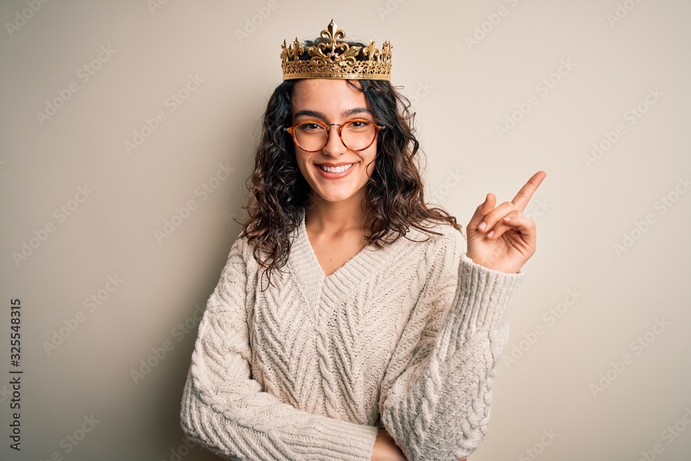 Young beautiful woman with curly hair wearing golden queen crown over ...