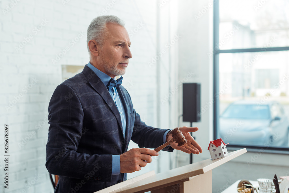 auctioneer pointing with hand at model of house and holding gavel ...