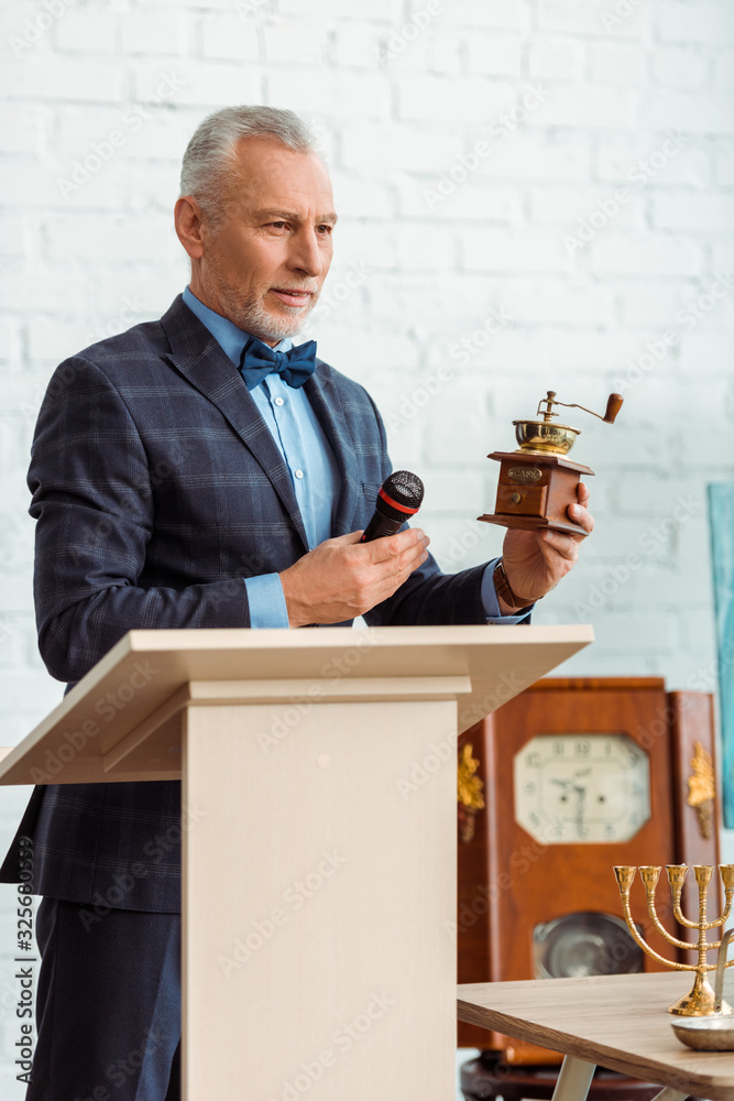 handsome auctioneer in suit pointing with hand at coffee grinder and ...