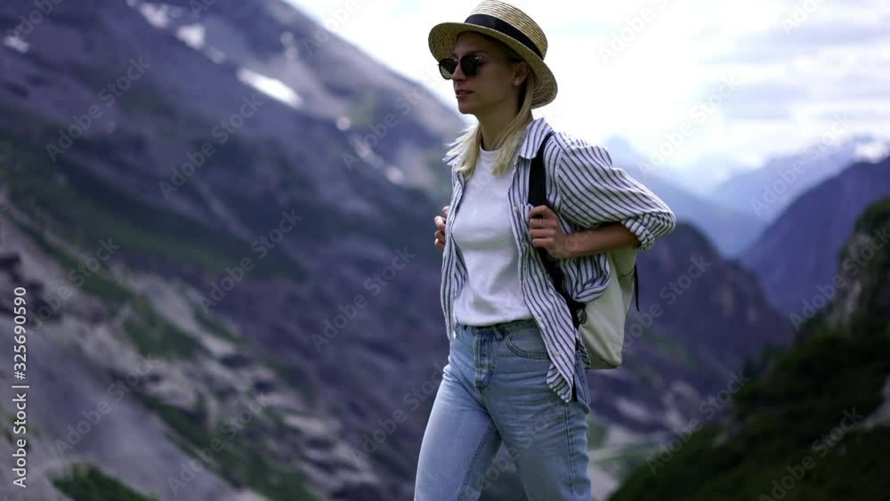 Smiling hipster girl in casual wear walking on path in Italian alps ...