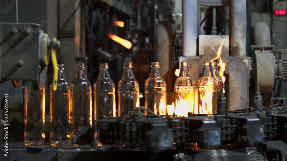 Glass bottles moving along a conveyor line fall under an open flame for ...