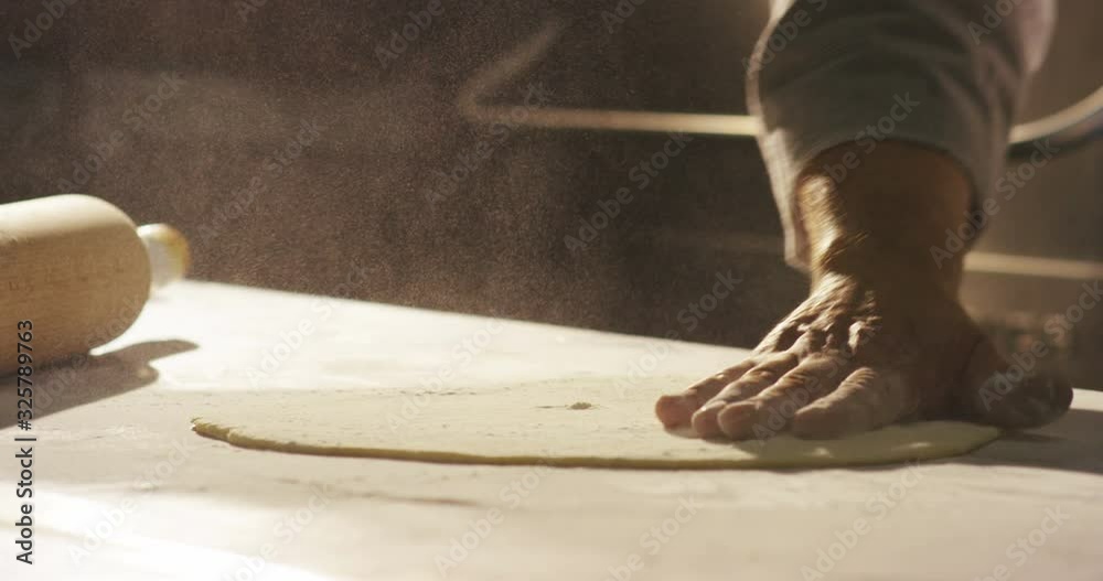 White flour flying into air as pastry chef in black suit slams ball ...