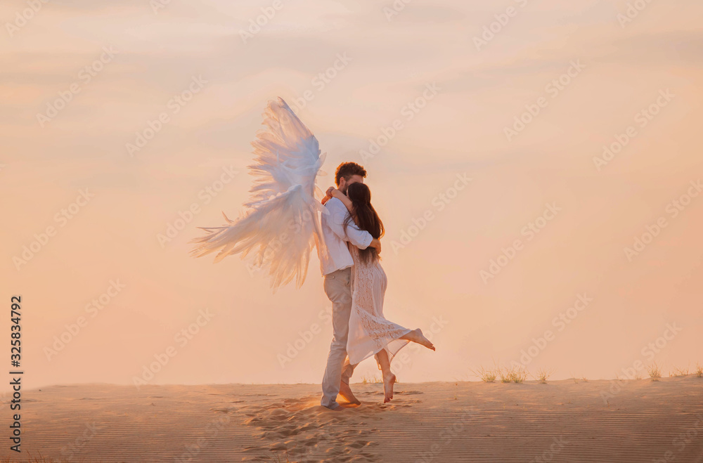 Girl and angel hugging. Brunette man in white suit with creative wings ...