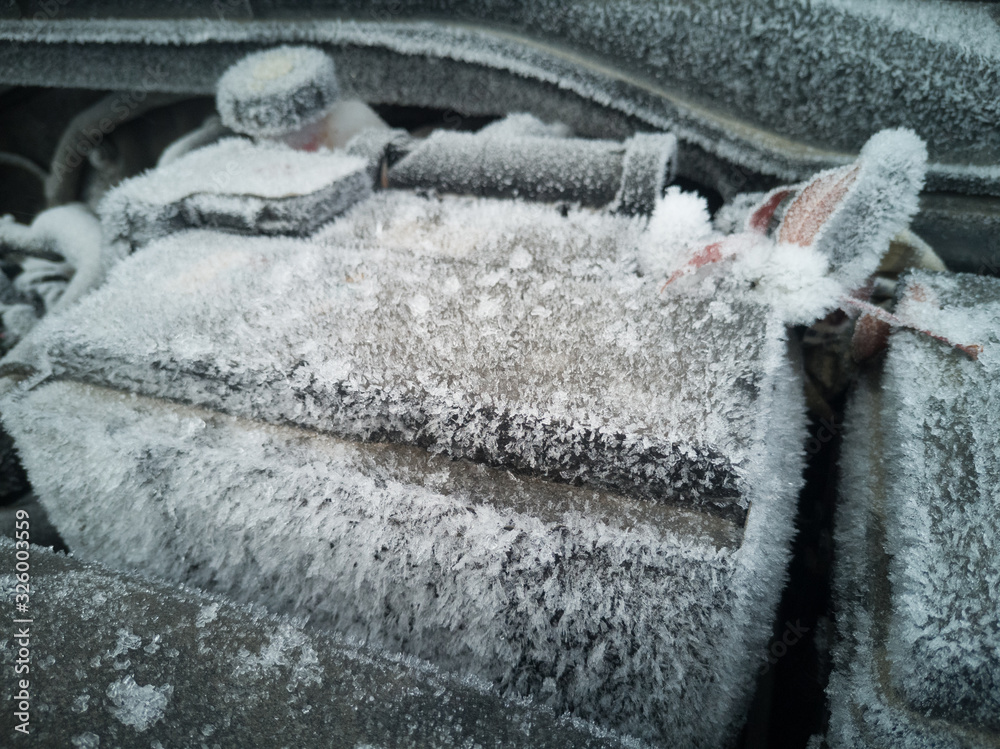 Car battery close-up. The engine compartment is covered with snow and ...