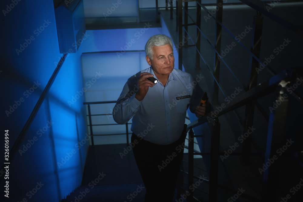 Professional security guard with flashlight on stairs in dark room ...