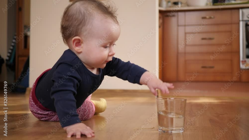 Toddler child awkwardly takes a glass of water and spills water on the ...