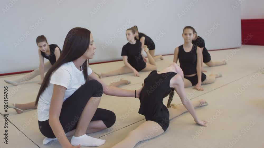 Tracking shot of female cheer coach helping preteen girls sitting in ...