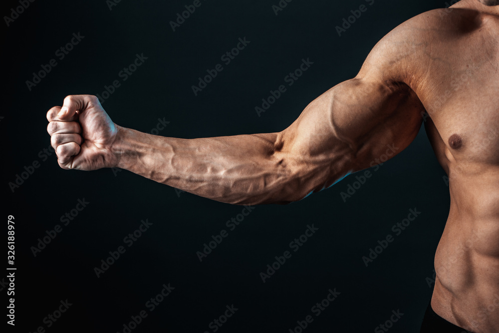 tense arm clenched into fist, veins, bodybuilder muscles on a dark ...