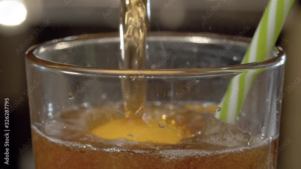 Close up cola fizzy drink pouring into the glass with ice and lemon on blurry lights background ...