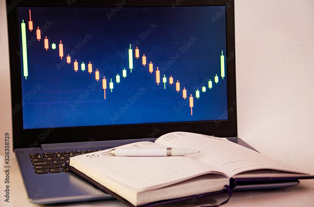 Trading on the exchange. Laptop on screen graph. Notepad pen rates ...