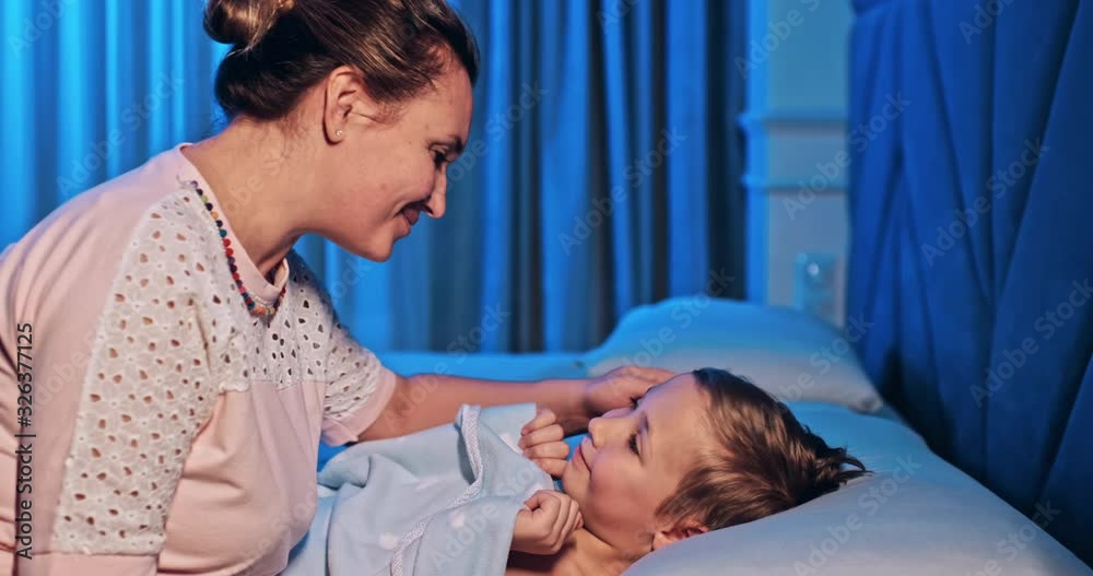 Mother puts the child to sleep sitting on the bed. Happy mom at crib of her son, who is ...