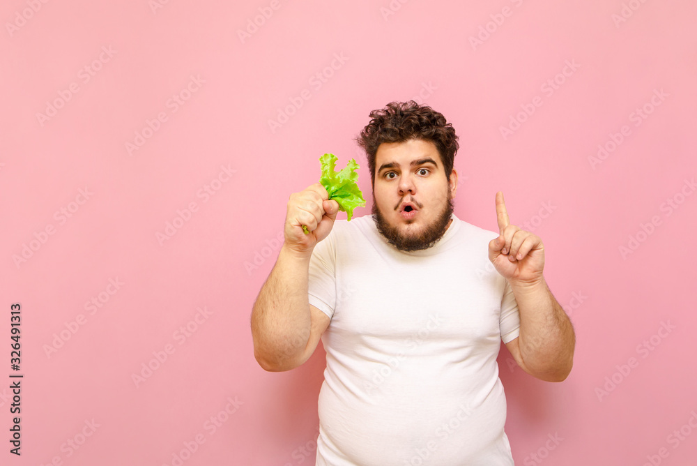Surprised fat young man with lettuce in his hand has an idea, looks ...