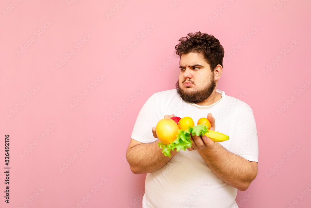 Funny fat guy with a serous face stands on a pink background, holds ...