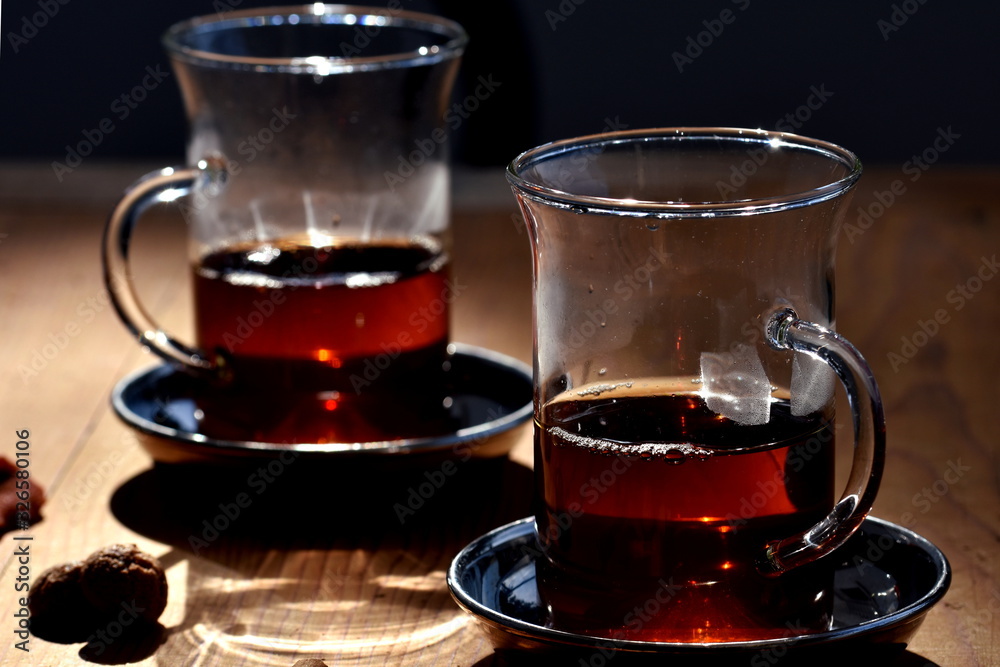 Hot golden amber dark tea in two tall glass mugs with handles on wooden ...