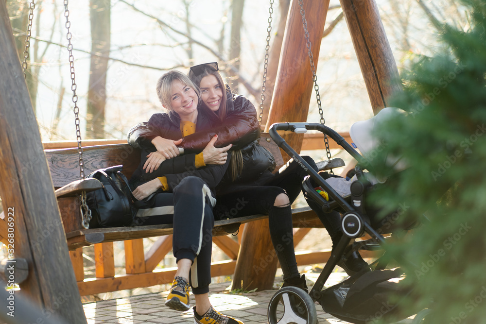 Happy mother with friend hugging at wooden Swing Seat In Garden with ...