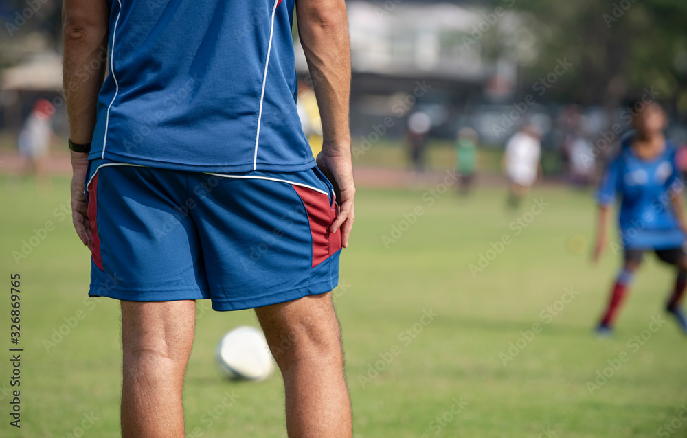 Male Youth Football Coach Standing And Watching His Team Playing In A School Tournament On A