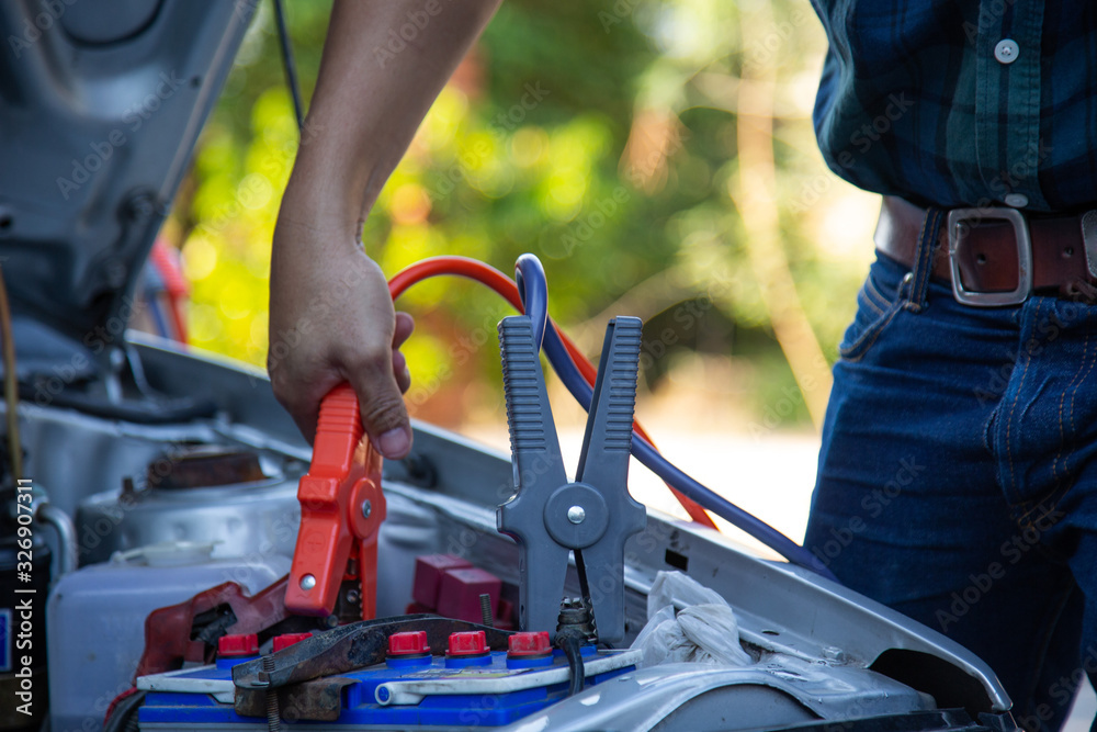 A man is using his hands to charge a car battery that is off because he ...