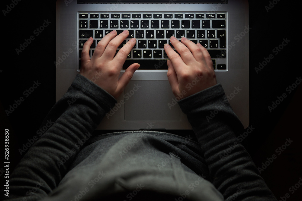 Overhead hacker in the hood working with laptop and mobile phone typing ...