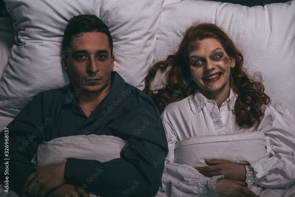 top view of female smiling demon lying in bed with frightened man Stock ...