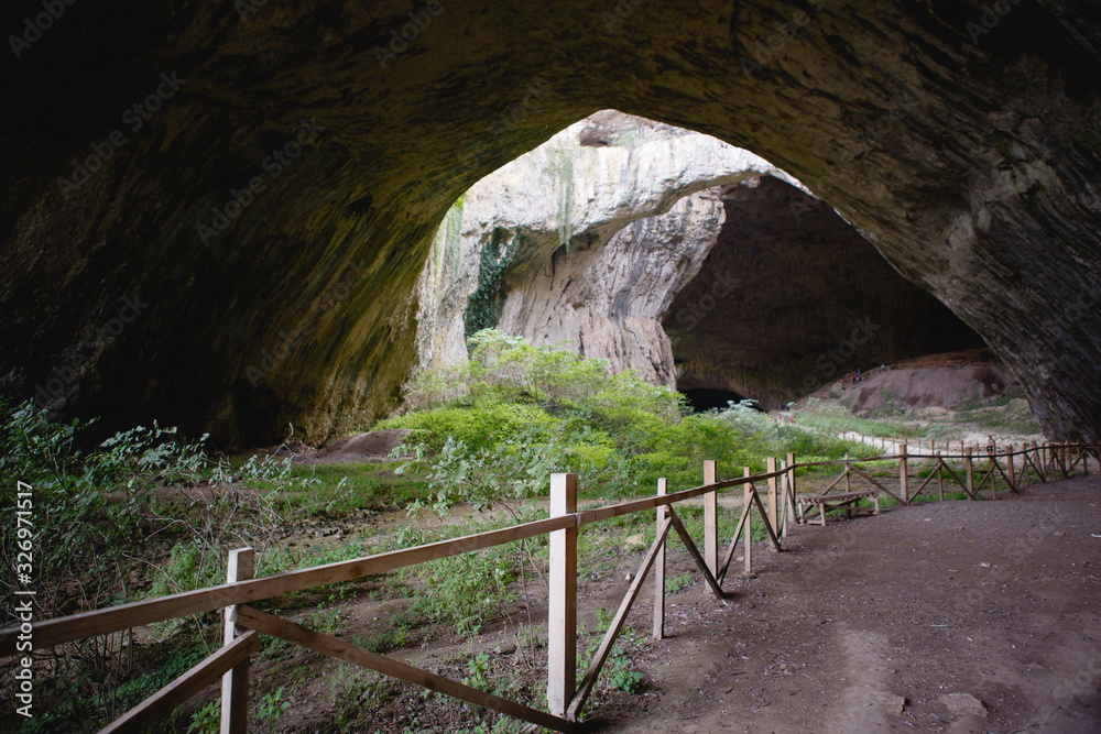 High arches of a huge stone cave with round holes at the top, a tourist ...