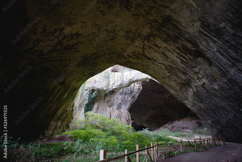 High arches of a huge stone cave with round holes at the top, a tourist ...