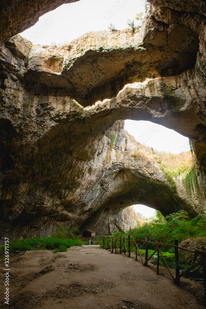 High arches of a huge stone cave with round holes at the top, a tourist ...