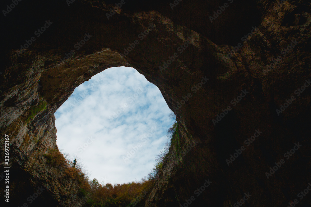 High arches of a huge stone cave with round holes at the top, a tourist ...