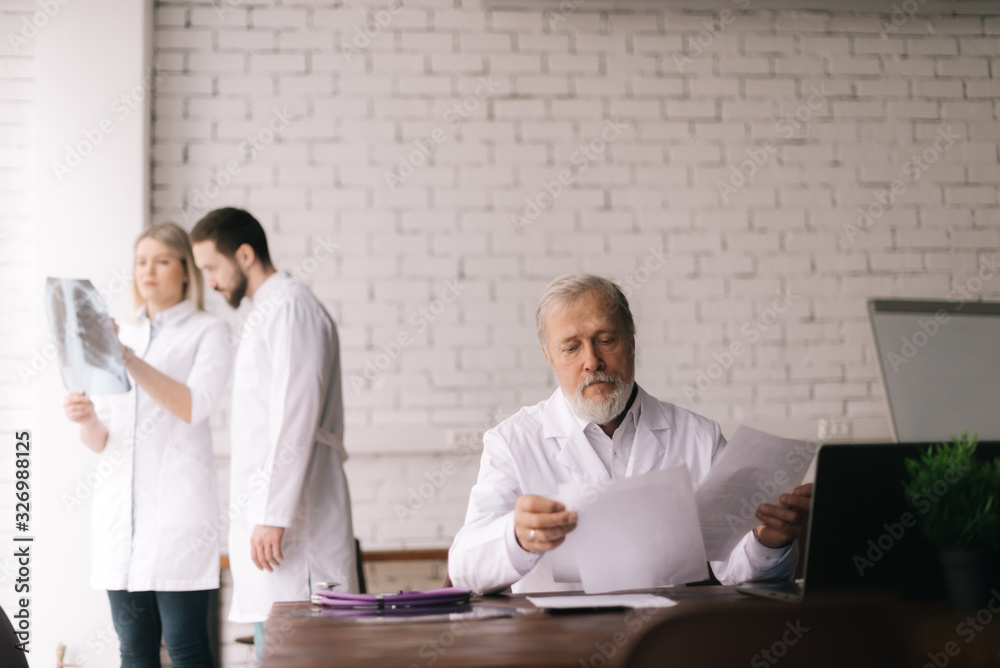 Experienced adult doctor sits at his desk and studies his patients ...