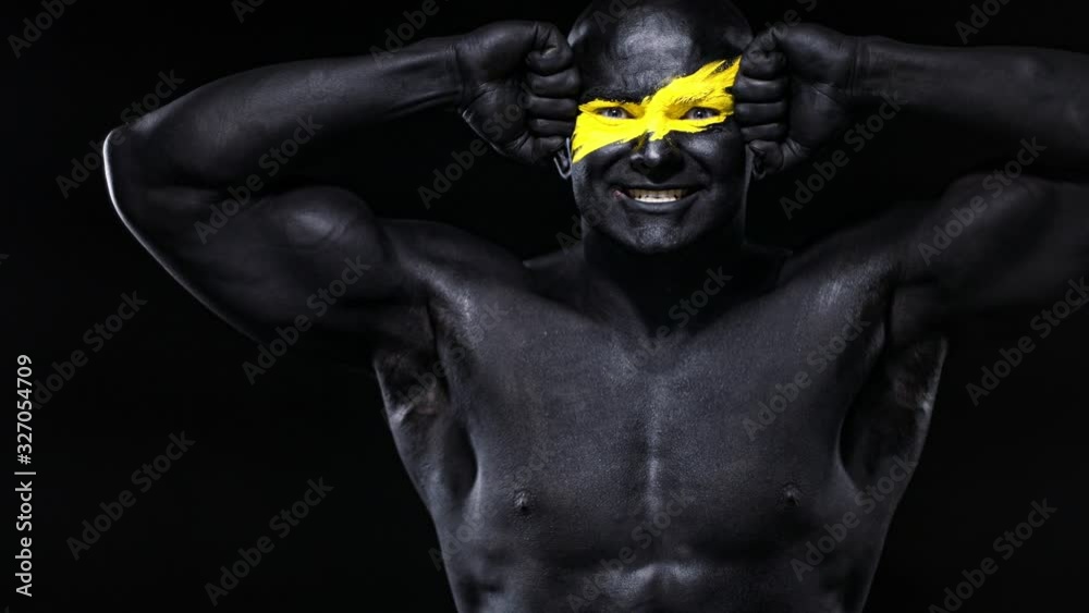 Man bodybuilder athlete with yellow color on face art and black body ...