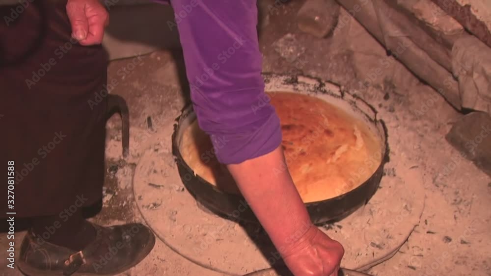 Old woman bakes bread under the peka. Making bread under the peka in ...