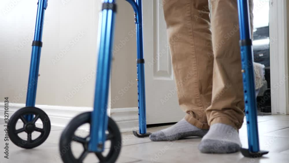 At home, a disabled older man walking with a walker slowly helped by ...