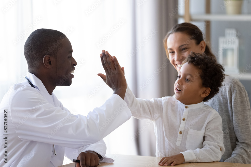 Friendly African American pediatrician doctor giving five to little boy ...