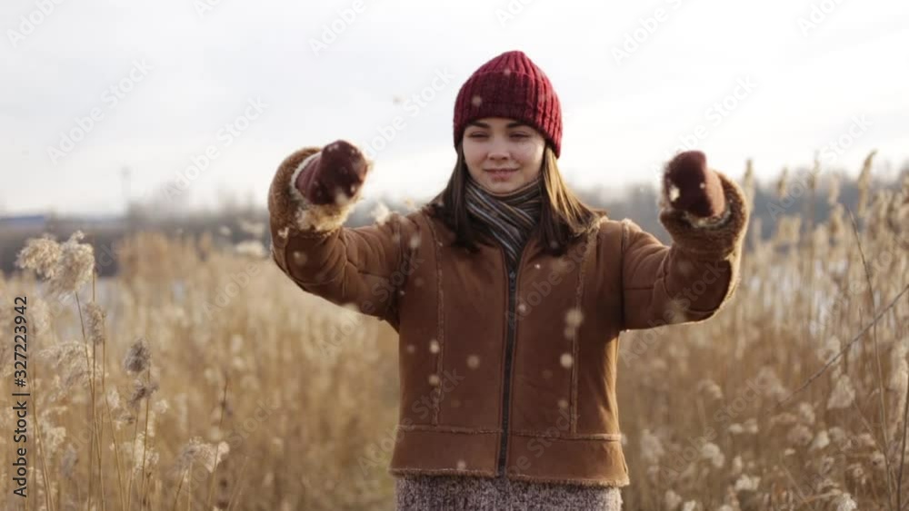 Young woman fluttering fluff in wind in field. Cheerful female standing ...