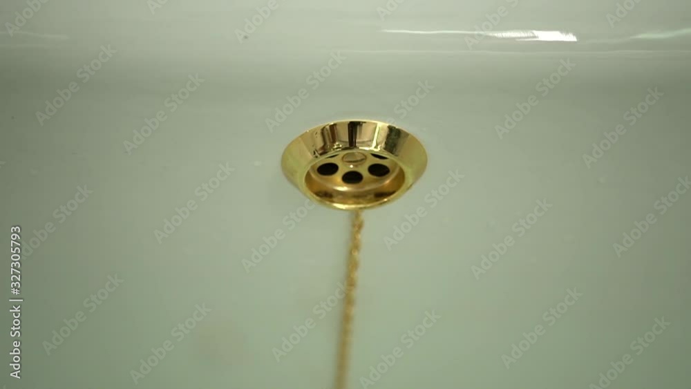 A golden-colored overflow opening with chain connected to tub drain ...