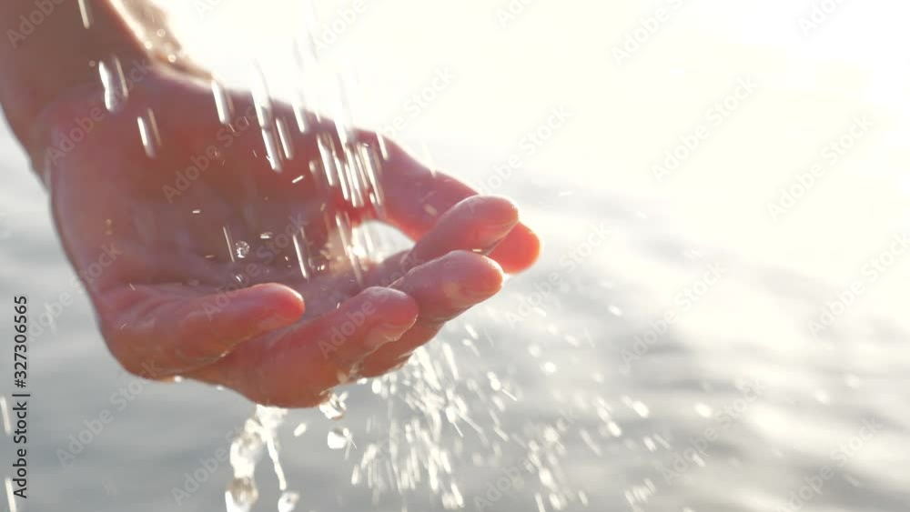 Womans cupped hand catches falling water drops on seascape background ...