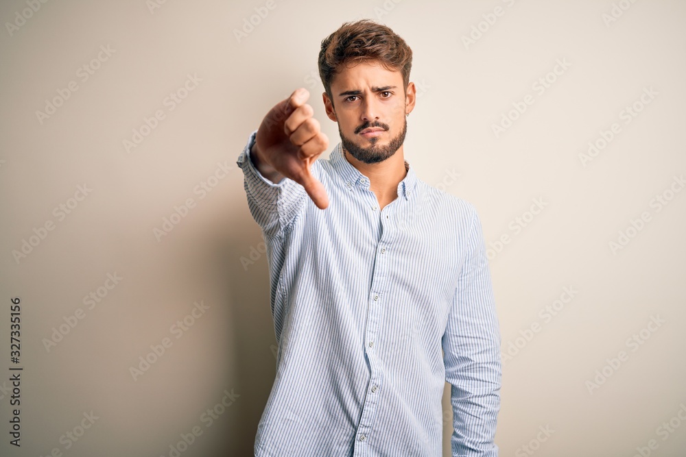 Young handsome man with beard wearing striped shirt standing over white ...