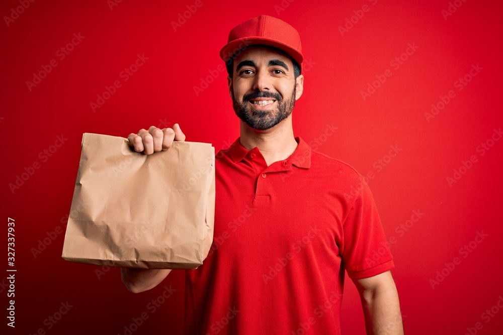 Young handsome delivery man with beard wearing cap holding takeaway ...
