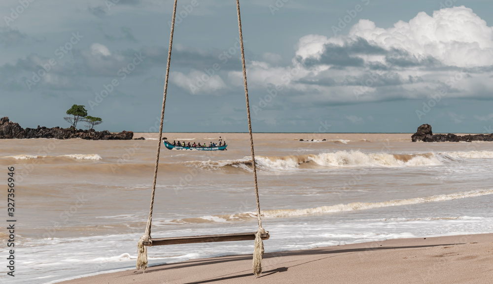 A hanging swing on an empty beach with a fishing boat in the background ...