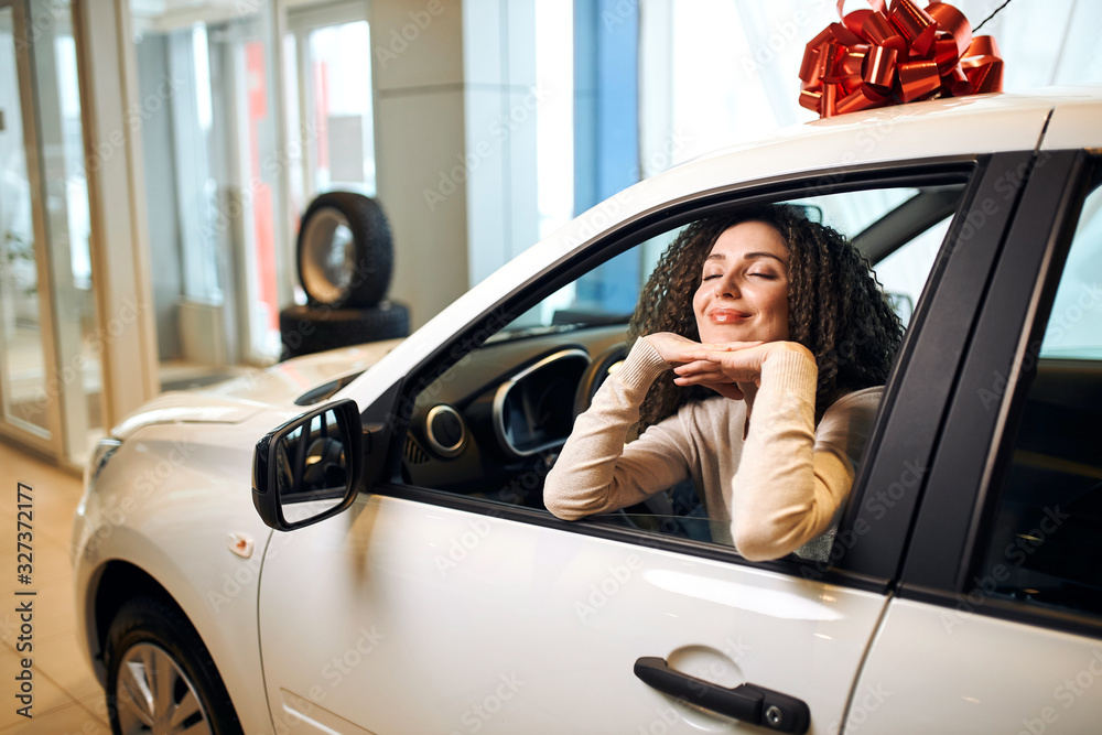 smiling happy woman with closed eyes leaning on the window of her car ...