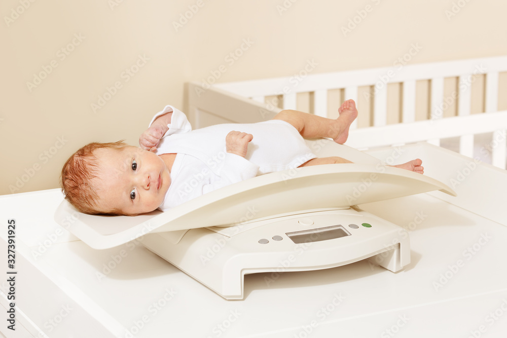Little baby boy lay on the scale for measuring body weight and looking ...