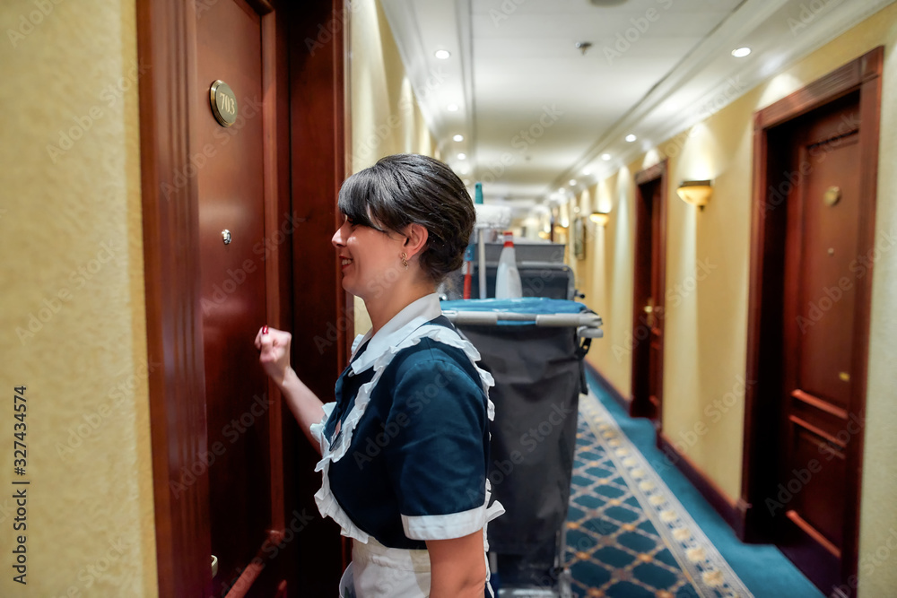 Let us clean. Smiling hotel maid in uniform knocking on the door for ...