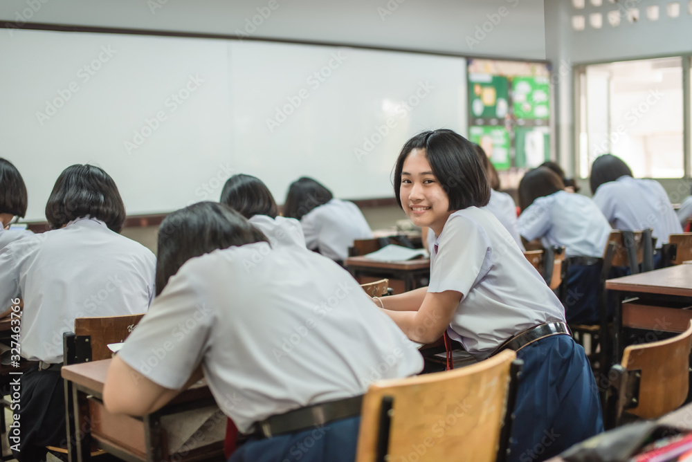 A pretty smiling Asian female student in white uniform is turning her ...