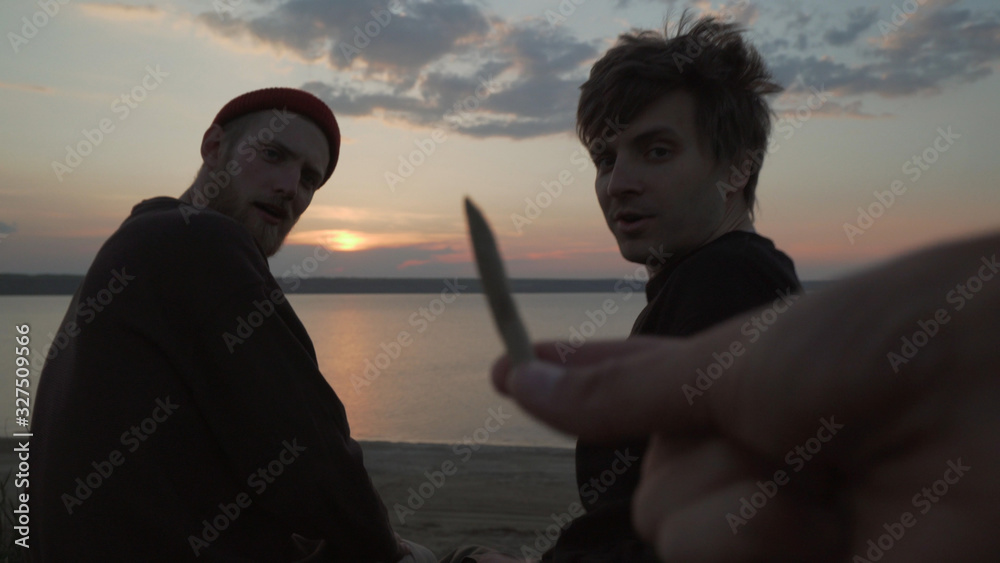 Hand from first person view offering smoking joint with weed to two ...