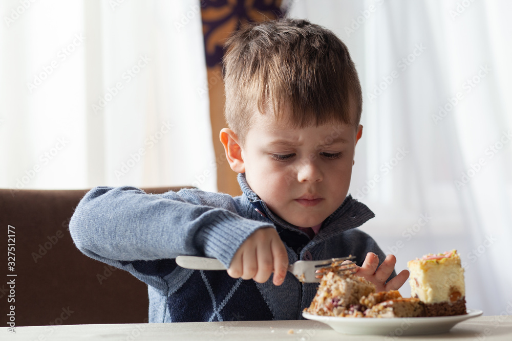Cute little boy in cafe eat a big piece of cake with a fork. Desserts ...