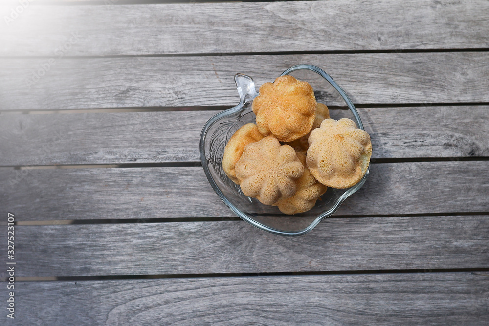 A bowl of Kuih Bahulu or Baulu on wooden table. Kuih Bahulu or Baulu is ...