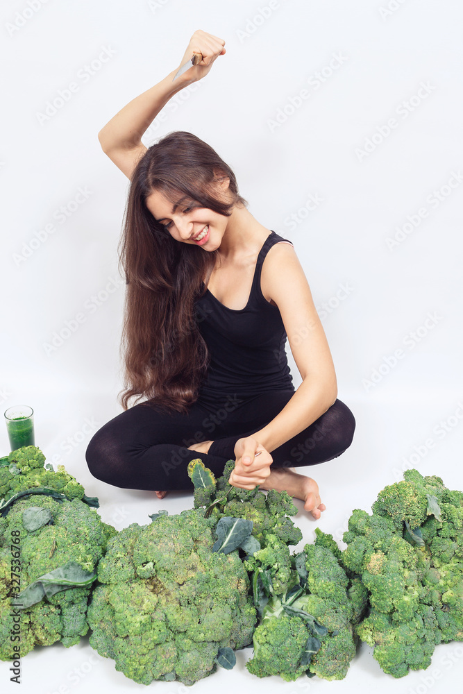 young beautiful girl sits in big heap of broccoli and pricks it on fork ...