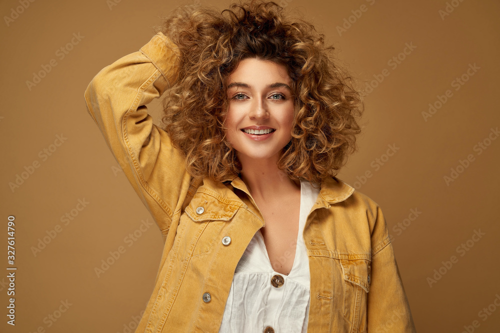Happy young woman with curls posing at studio on brown studio ...