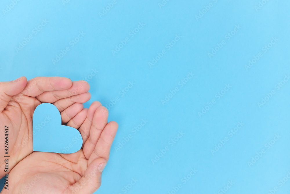 Blue heart shape cutout on hands in blue background. Top view, kindness ...